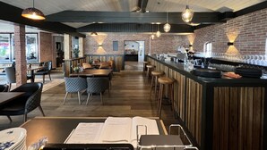 Um restaurante com parede de tijolos, teto de madeira e um bar com banquetas e balcão.