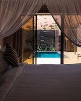 Quarto com uma cama grande, vista para uma piscina e cerca de madeira na parte externa.