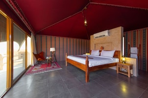 Um quarto espaçoso com uma cama grande, uma mesa de cabeceira, uma luminária e vista para o exterior através de amplas janelas.