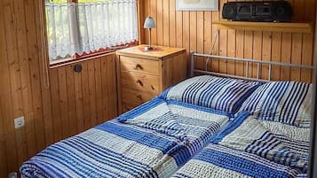 Um quarto com painéis de madeira, uma cama, uma mesinha, um abajur e um quadro na parede.