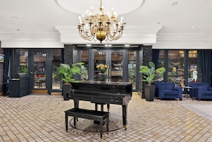 Um hall de entrada com um piano de cauda, um candelabro e plantas em vasos.