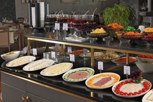 Buffet com diversos alimentos, incluindo queijos, carnes, frutas e legumes.