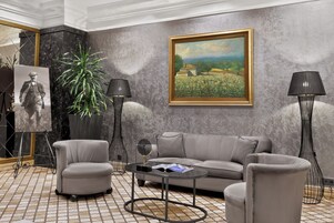 Uma sala de estar moderna com um sofá cinzento, duas poltronas, uma mesa de centro, um abajur, um quadro, uma planta em vaso e uma fotografia emoldurada.