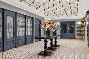 Um hall com piso de azulejos, uma mesa preta com um vaso de flores e um teto com luminárias pendentes.
