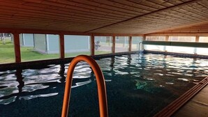 Piscina interna com teto de madeira e paredes de vidro transparente.