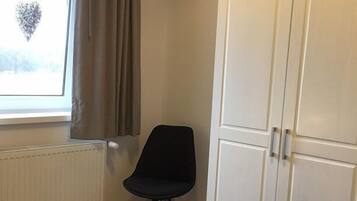 Quarto com janela, radiador, cadeira preta e armários brancos.