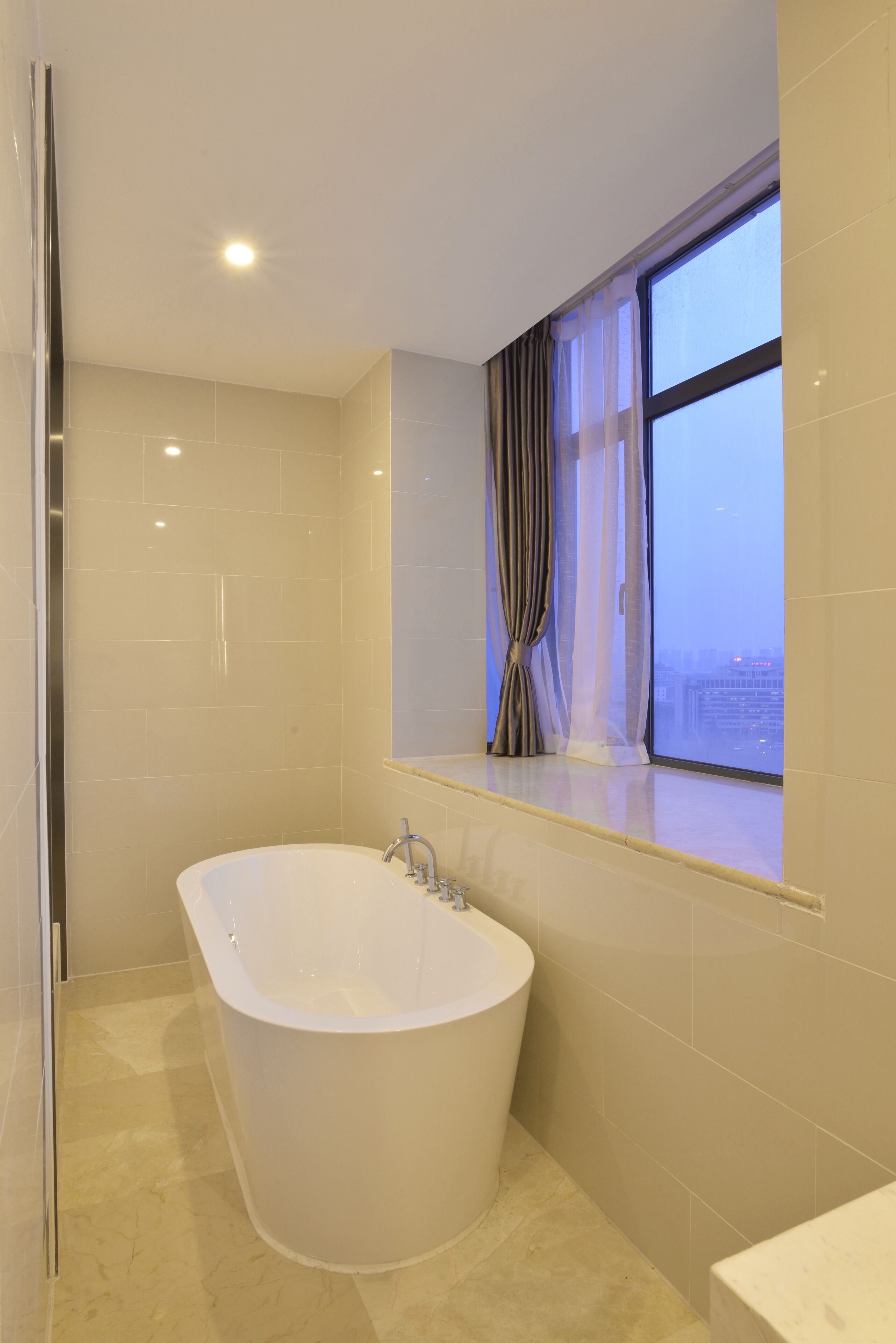 Um banheiro moderno com uma banheira independente, uma janela grande com cortinas e vista para a cidade.