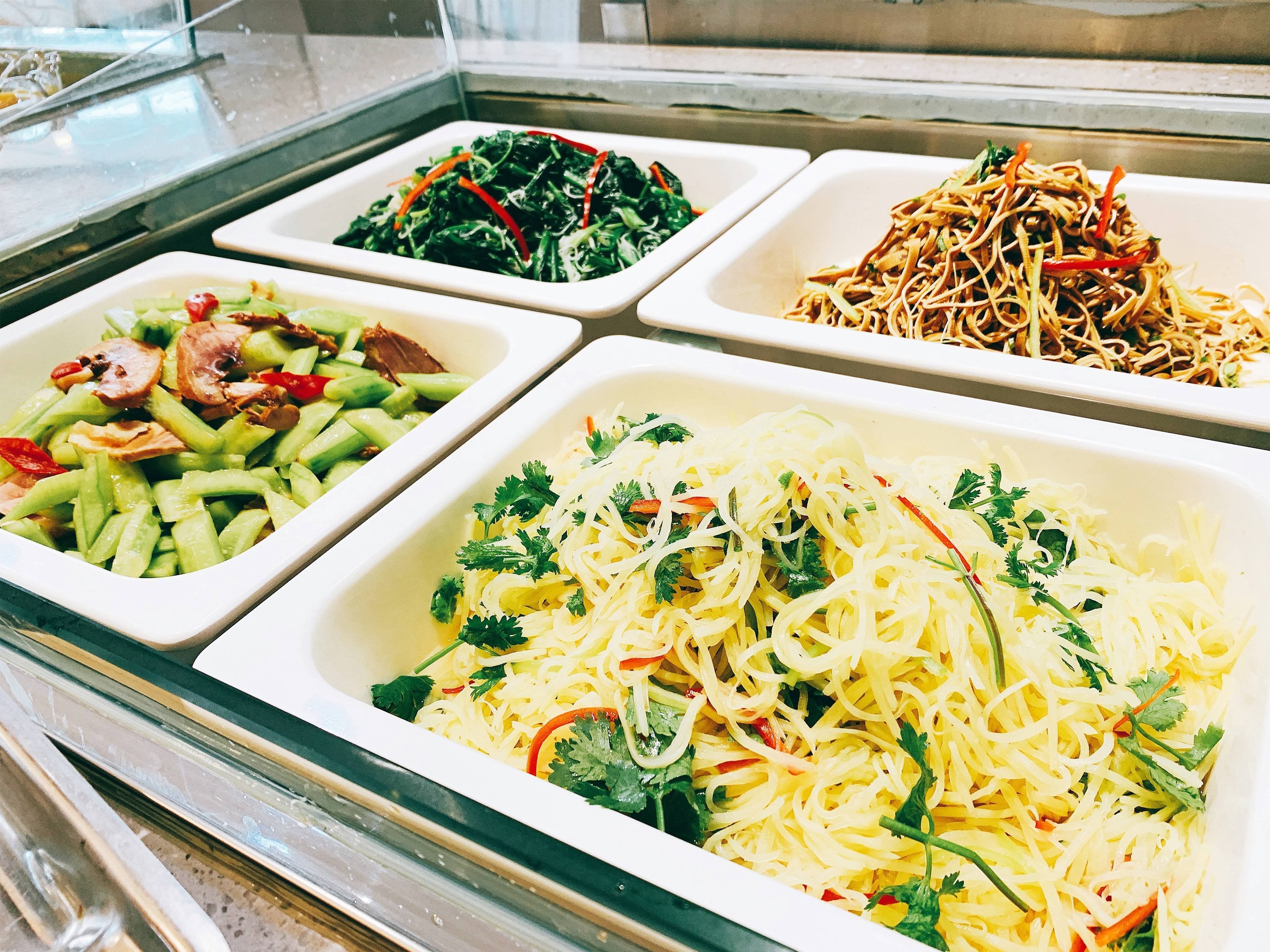Buffet com diversos pratos, incluindo macarrão, legumes e carnes.