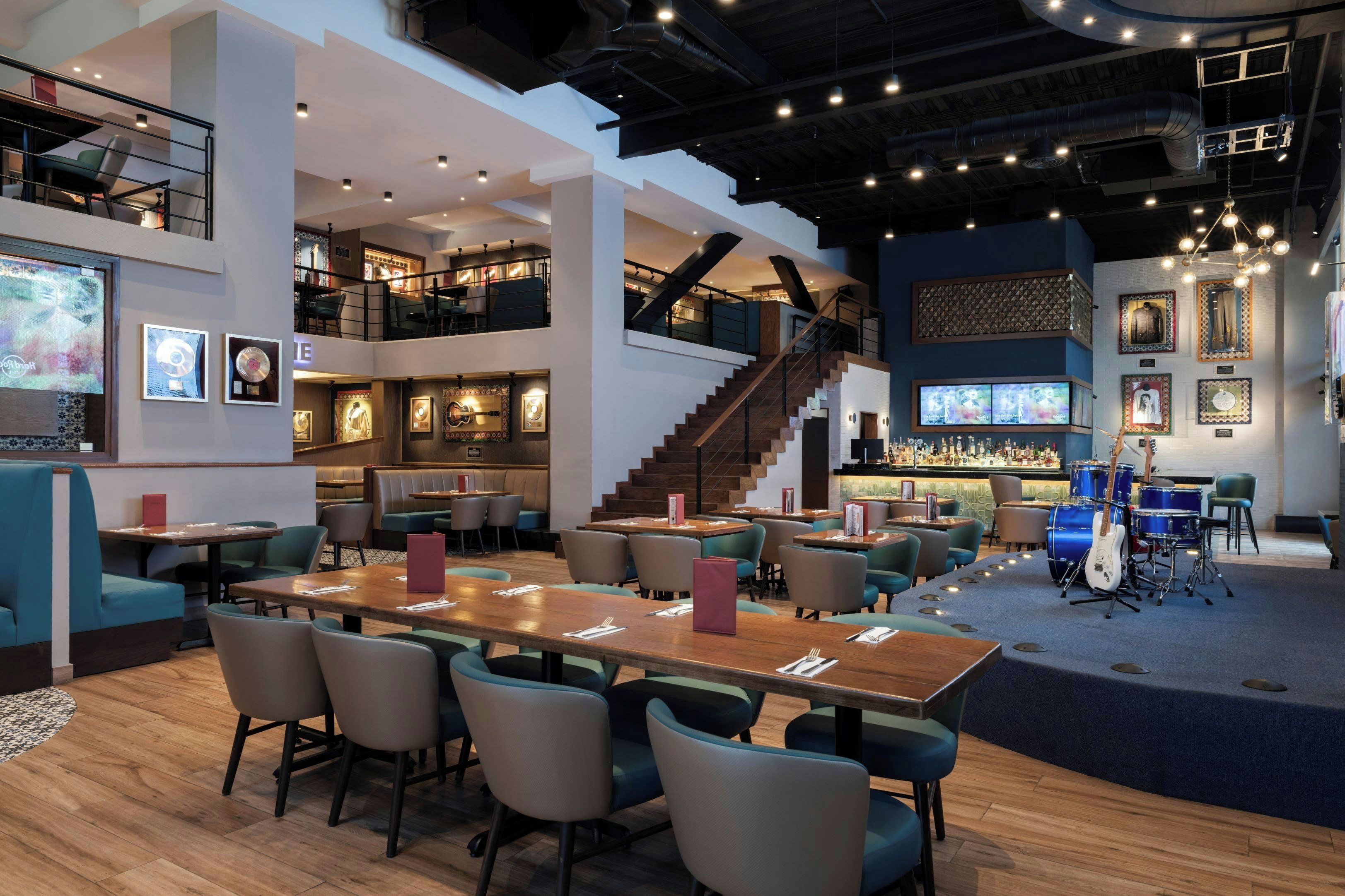 Restaurante em vários níveis com mesas e cadeiras de madeira, área de bar e palco com instrumentos musicais.