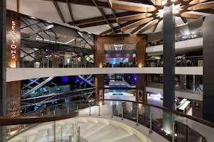 Um shopping center com vários níveis, corrimãos de vidro, vigas de madeira e um átrio central.