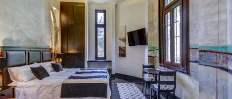 Quarto com uma cama grande, uma escrivaninha e uma televisão.
