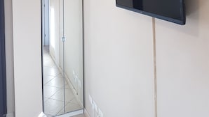 Quarto com televisão montada na parede, porta de correr de vidro que dá para um banheiro e ar-condicionado na parede.