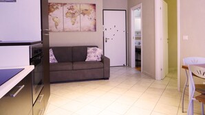 Um espaço compacto com cozinha compacta, um sofá com almofadas estampadas, uma obra de arte com mapa-múndi e uma porta que dá para o banheiro.