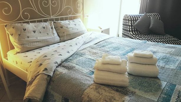 Uma cama bem arrumada com um edredom estampado, almofadas com desenhos de coração e toalhas dobradas sobre a cama.