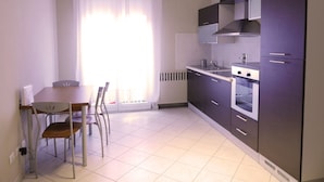Cozinha compacta com área de jantar, apresentando uma mesa, cadeiras, fogão e geladeira.