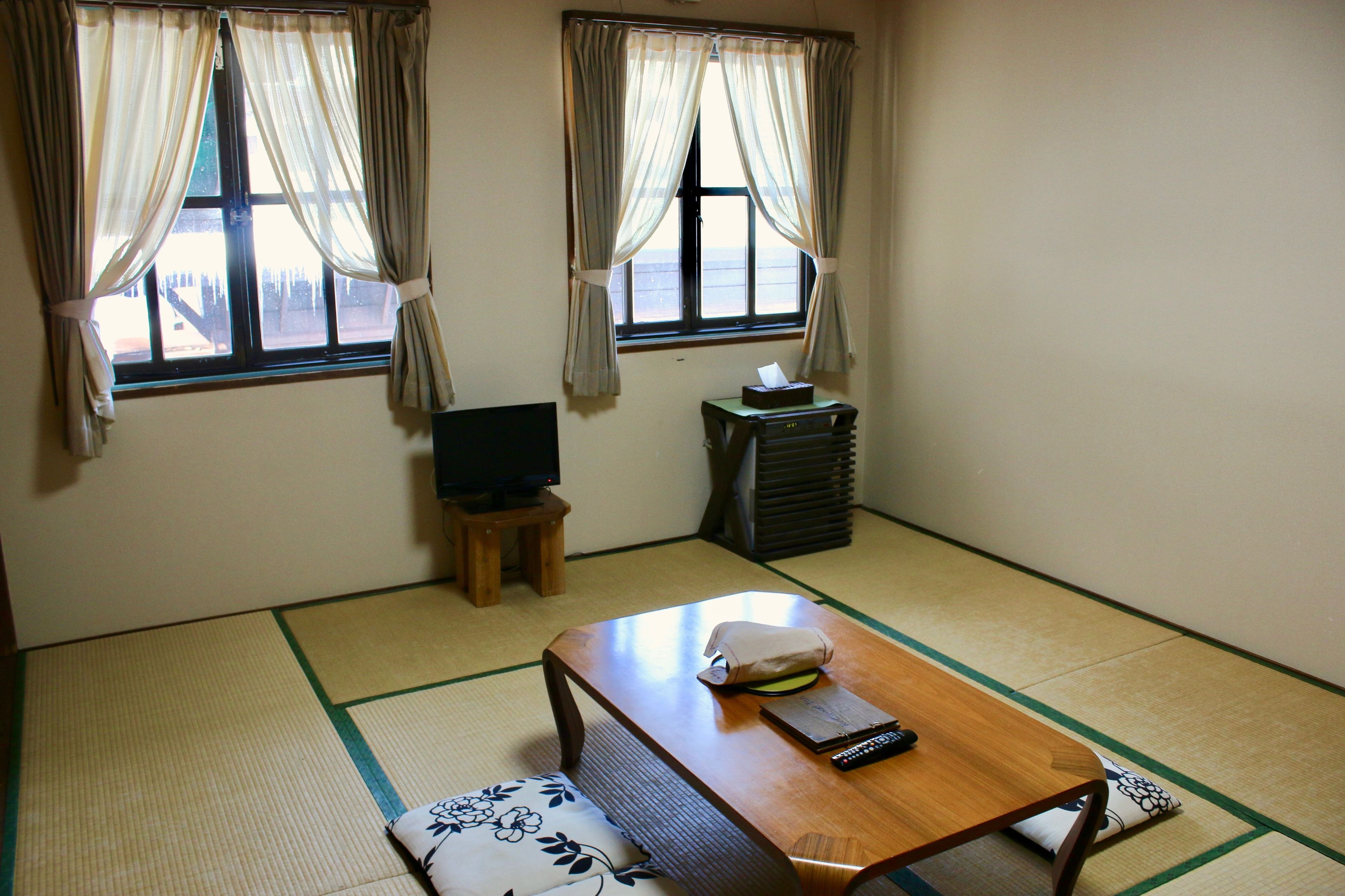 Um quarto japonês tradicional com tatames, uma mesa de madeira baixa, uma televisão sobre um banquinho pequeno e uma cama futon.