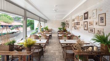 Restaurante com mobiliário de vime, paredes de tijolo branco e quadros emoldurados.