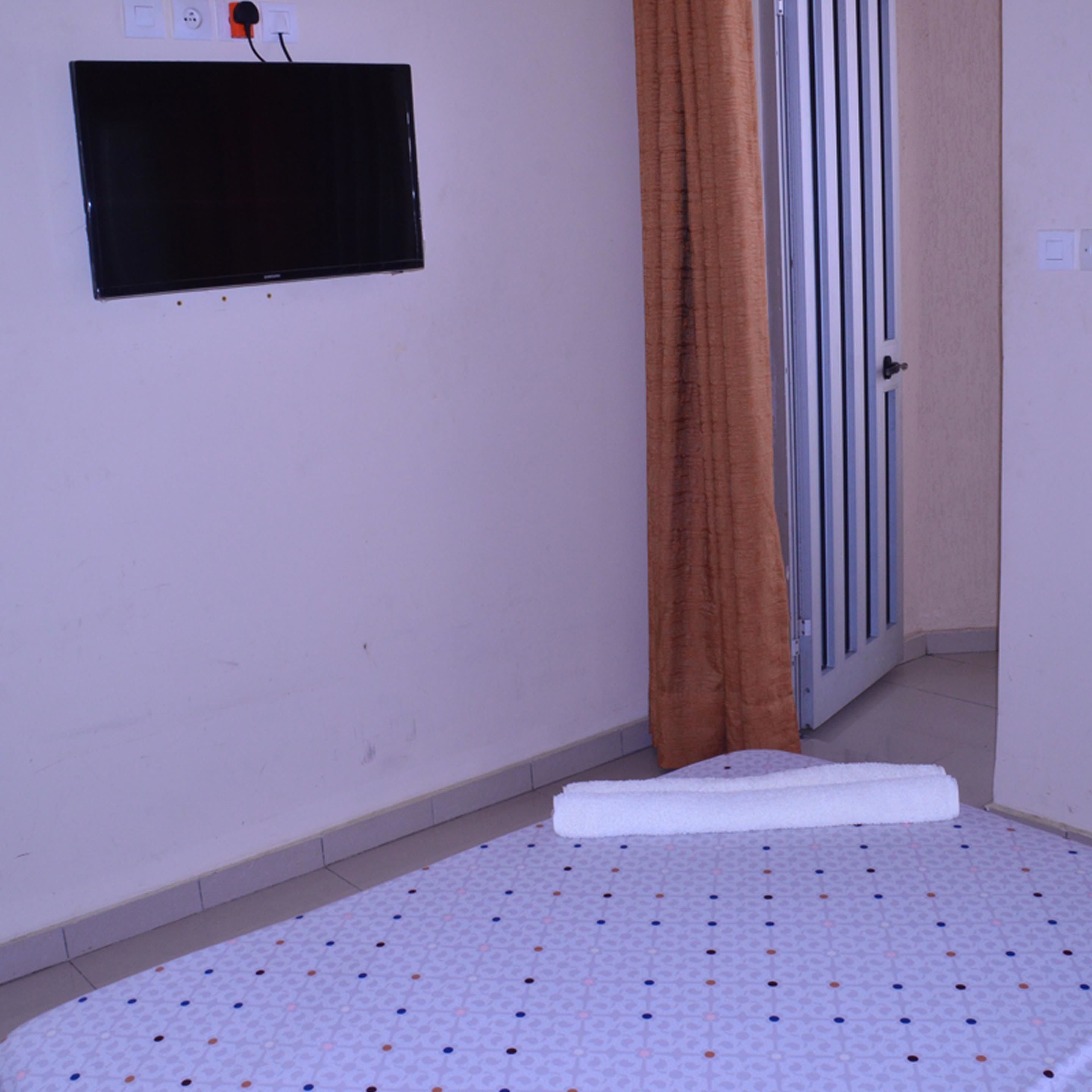 Quarto com cama, televisão de tela plana na parede, porta com puxador de metal e cortina.