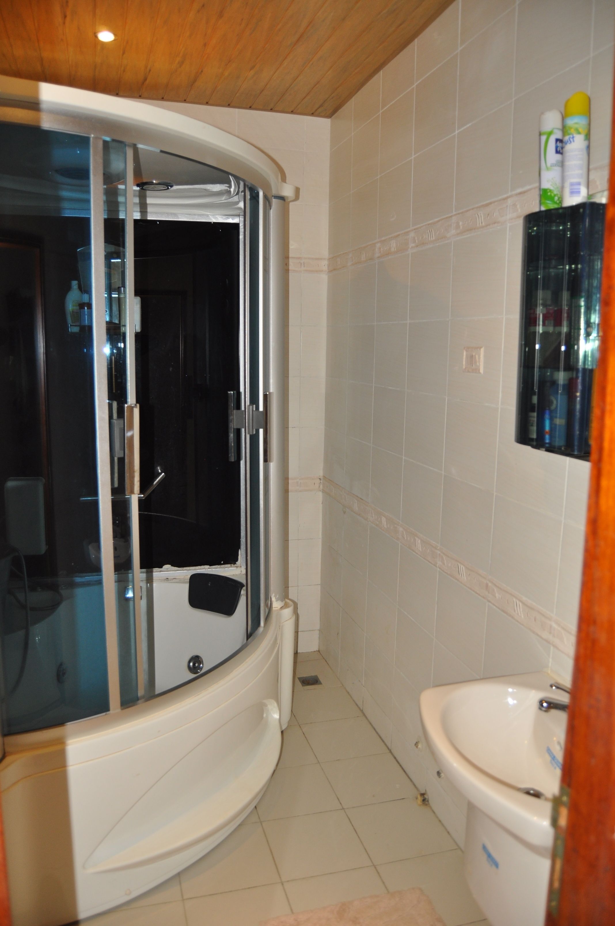 Casa de banho com cabine de duche em vidro, lavatório branco e parede revestida a azulejos.