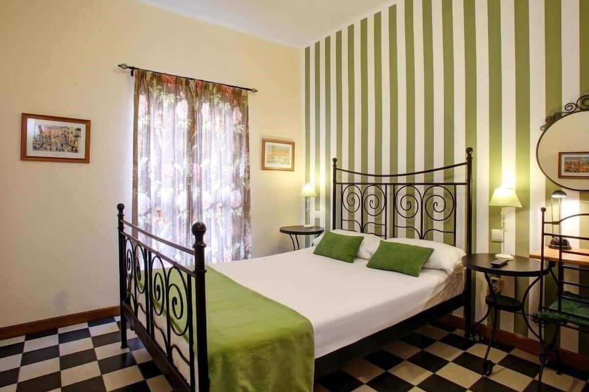 Quarto com cama, piso xadrez, parede listrada e janela com cortinas.