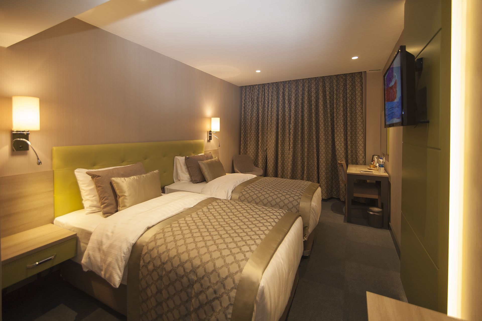 Quarto de hotel com duas camas, uma escrivaninha, uma cadeira e uma televisão.