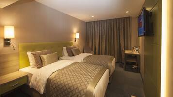 Quarto de hotel com duas camas, uma escrivaninha, uma cadeira e uma televisão.