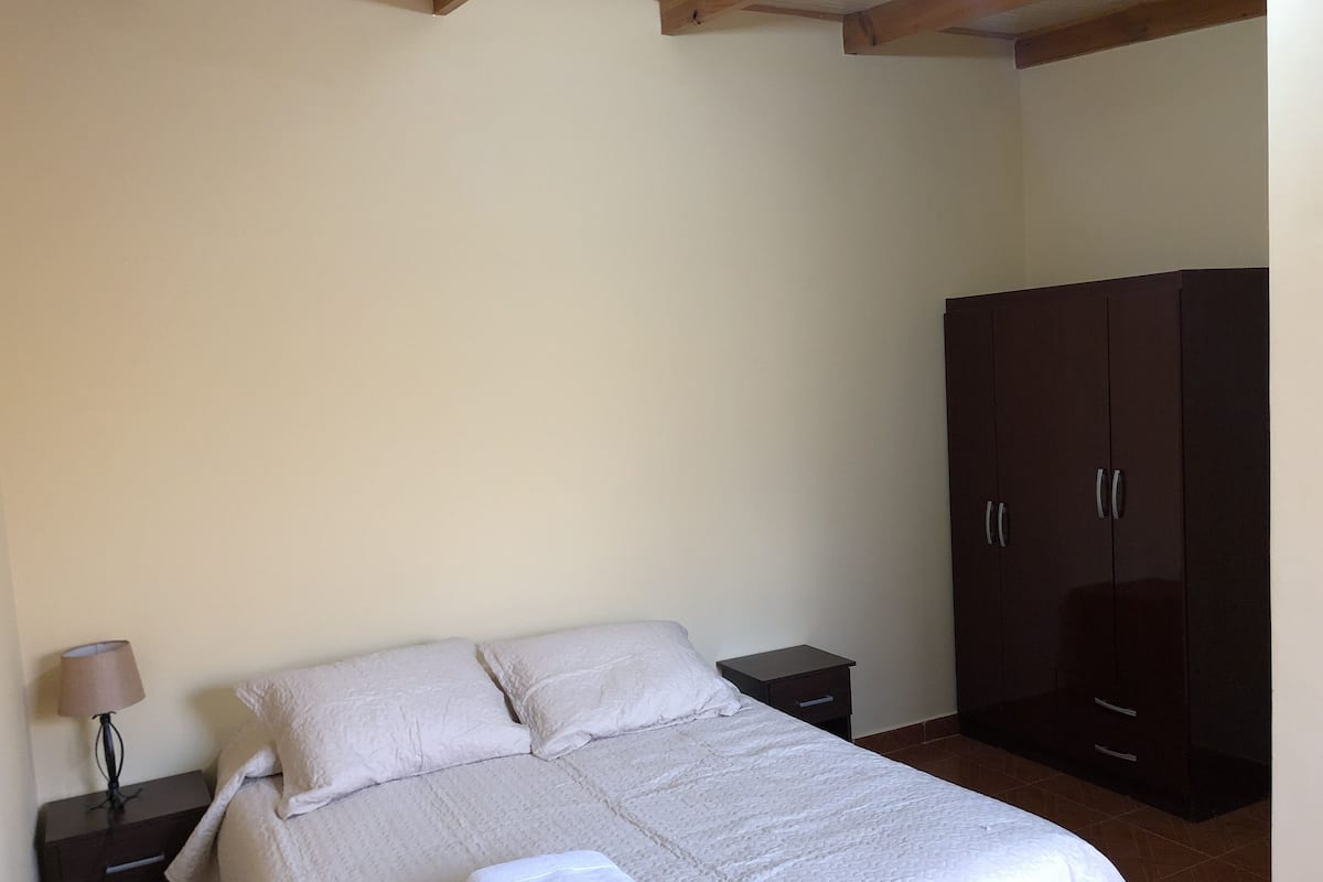 Um quarto com uma cama, uma mesa de cabeceira, um abajur e um guarda-roupa.