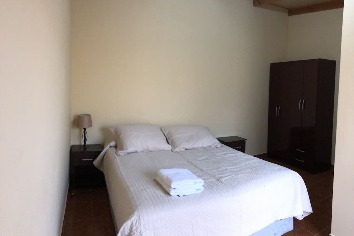 Quarto com uma cama, mesa de cabeceira, luminária e guarda-roupa.