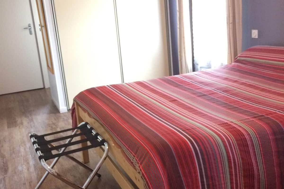 Um quarto com uma cama, uma janela com cortinas, uma porta e um radiador.