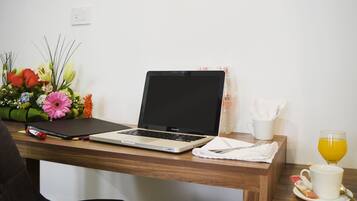 Uma escrivaninha de madeira com um laptop, um buquê de flores, uma xícara de café, um copo de suco de laranja e um guardanapo.