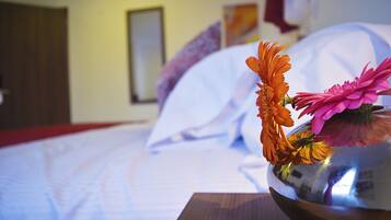 Quarto de hotel com uma cama, uma mesa de cabeceira de madeira e um vaso com flores.