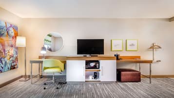 Quarto de hotel com escrivaninha, cadeira, televisão, obras de arte e micro-ondas.