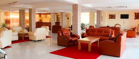 Um hall amplo com sofás e poltronas de couro, um balcão de recepção e um tapete vermelho.