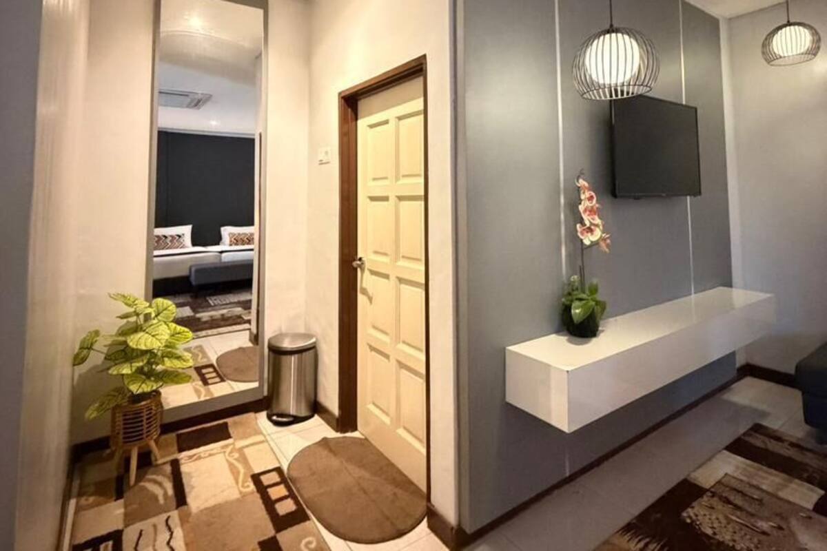 Um corredor moderno com um espelho, uma lixeira, uma planta em vaso, um banco e uma TV na parede.