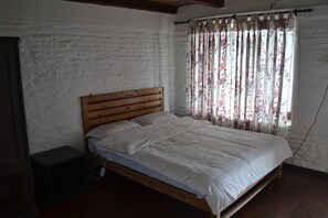 Quarto com cama de madeira, paredes brancas e janela com cortinas florais.