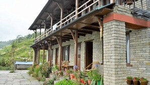 Um edifício de pedra com varanda, rodeado por plantas em vasos.