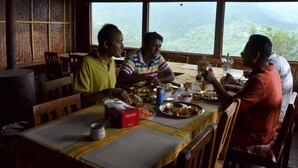 Uma sala de jantar com mesa posta para três pessoas, móveis de madeira e vista para as montanhas através de grandes janelas.