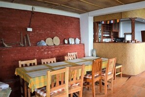 Uma sala de jantar com parede vermelha, cadeiras de madeira e mesa com toalha xadrez.