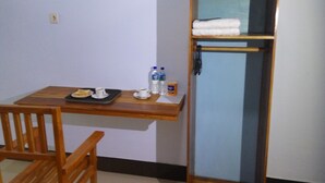 Um quarto pequeno com uma mesa de madeira, uma cadeira, um armário com espelho e uma estante com toalhas.