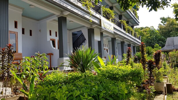 Um edifício com varanda coberta, colunas e um jardim com diversas plantas.