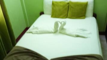 Cama bem arrumada com edredom branco e marrom, duas almofadas e uma toalha dobrada em formato de coração.