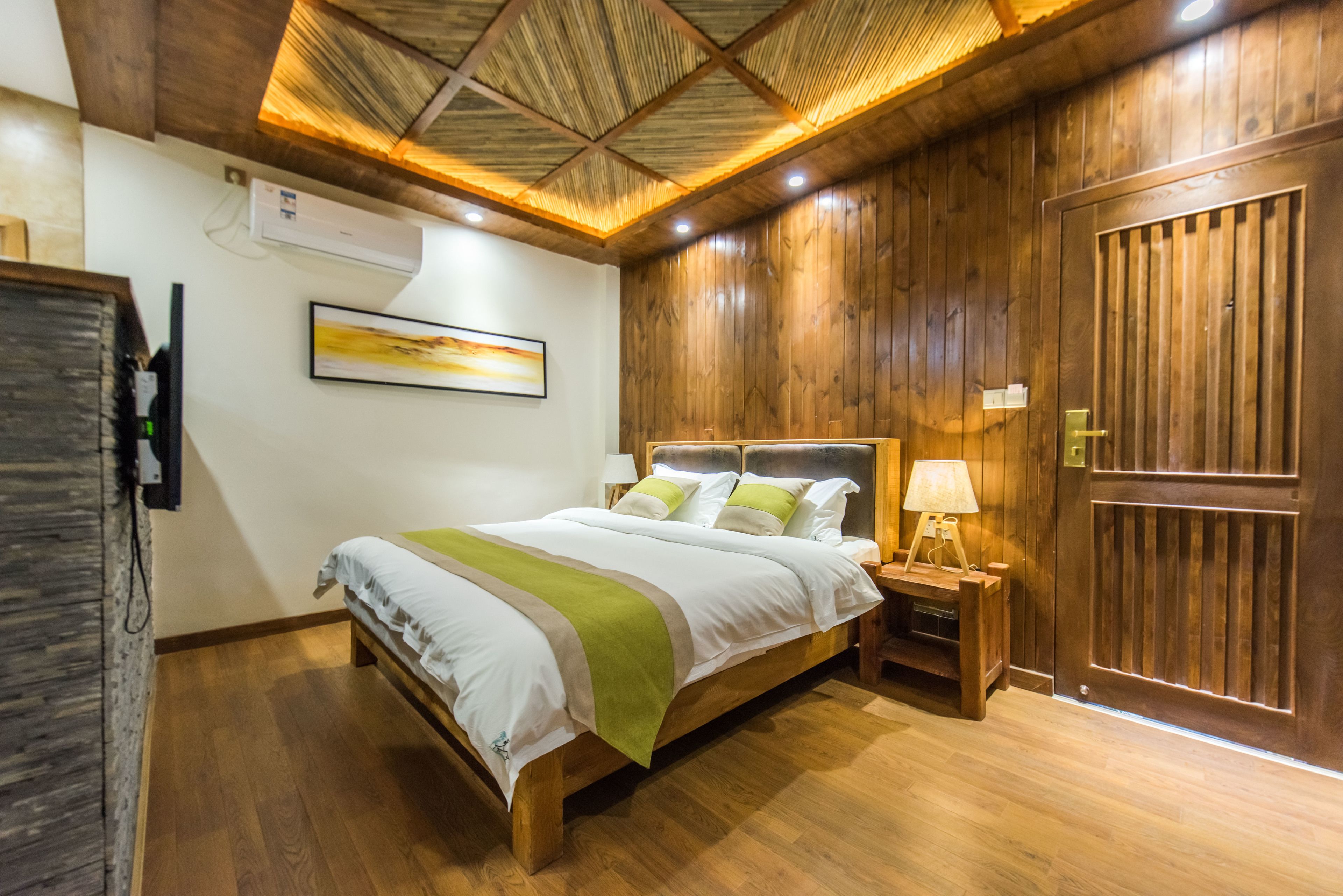 Quarto com painéis de madeira, uma cama, mesa de cabeceira, abajur e porta.
