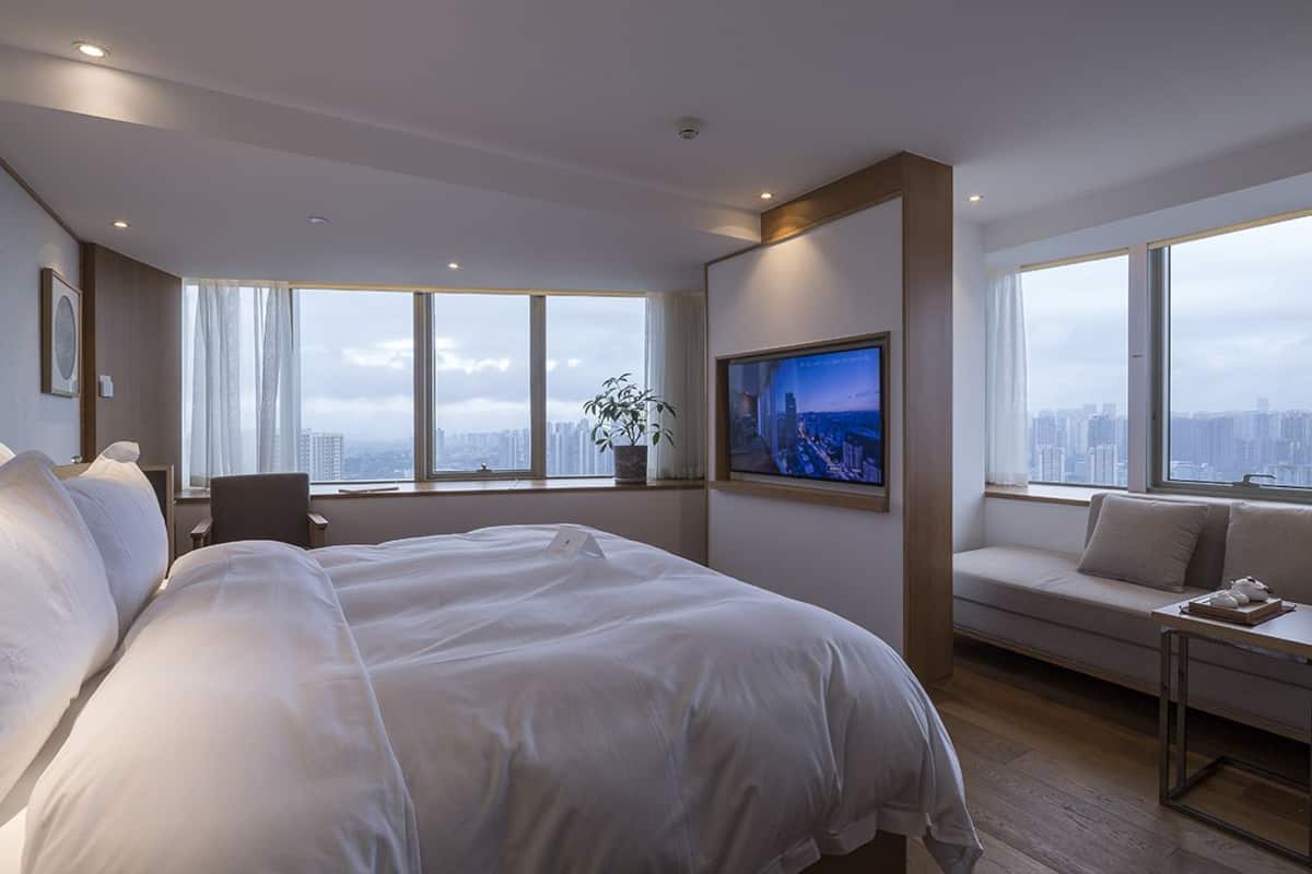 Quarto de hotel moderno com uma cama grande, um sofá, uma TV e vista para a cidade.