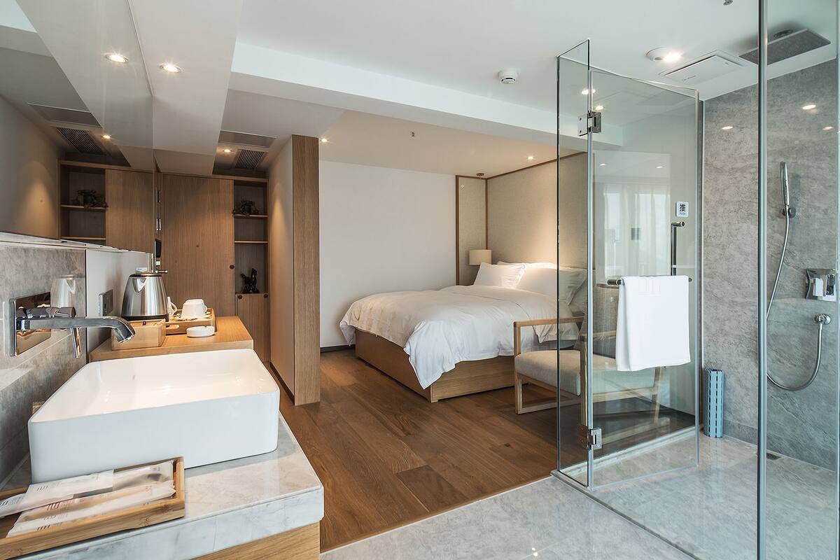 Quarto de hotel moderno com banheiro espaçoso, chuveiro independente, cama e armário embutido.