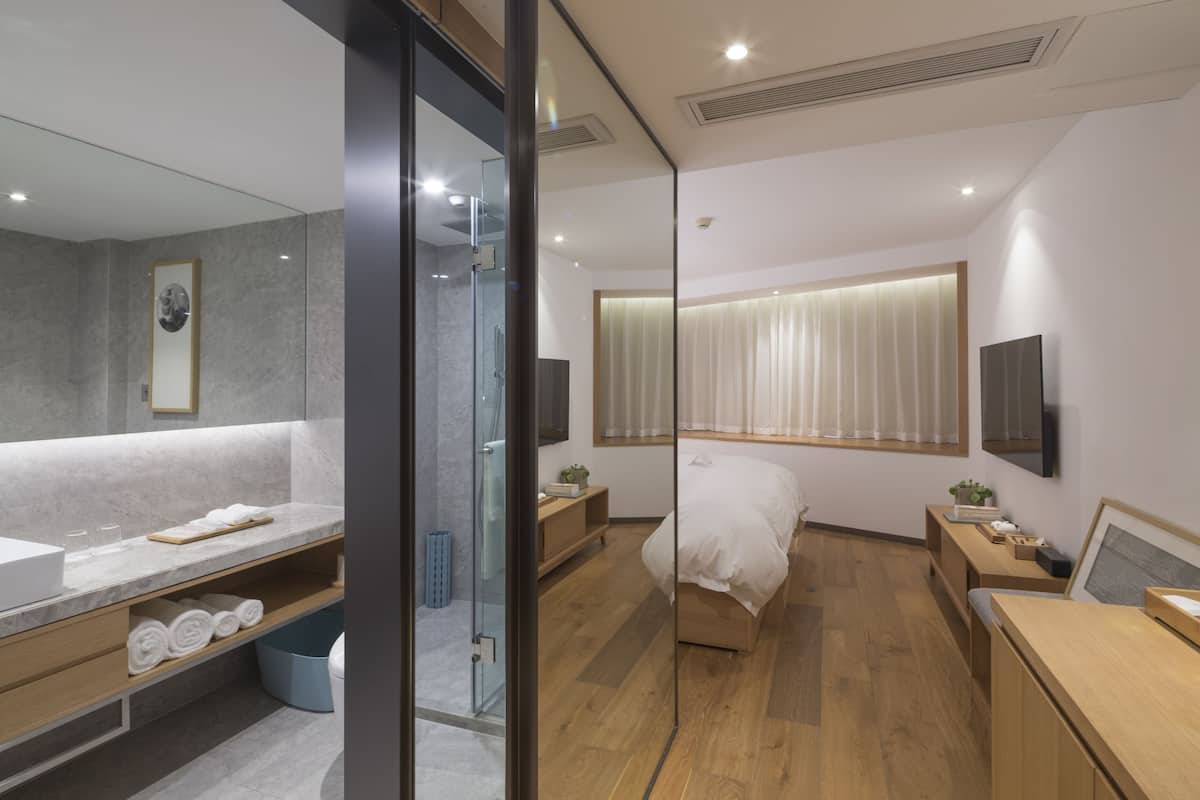 Quarto moderno com cama grande, mesa de cabeceira, espelho e janela com cortinas.