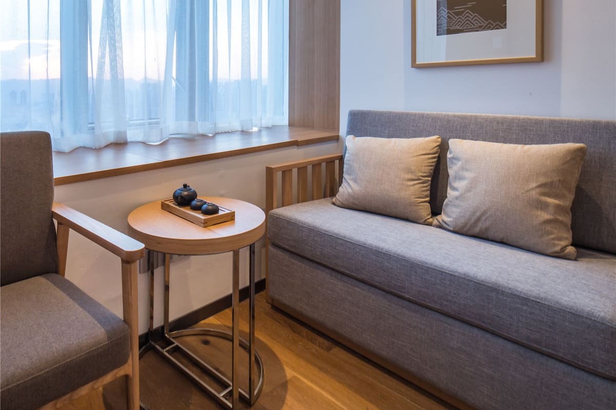 Uma sala de estar moderna com um sofá cinzento, uma mesinha redonda com um bule e cortinas leves.