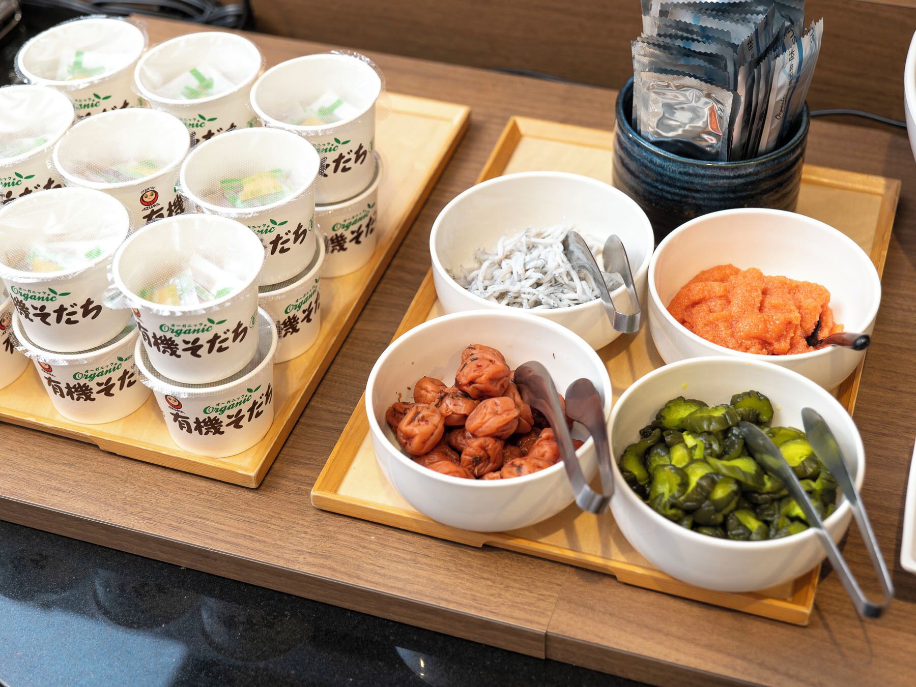 Uma mesa com diversos alimentos e recipientes, incluindo tigelas de vegetais, um prato de amendoins e vários copos com um logotipo de folha verde.