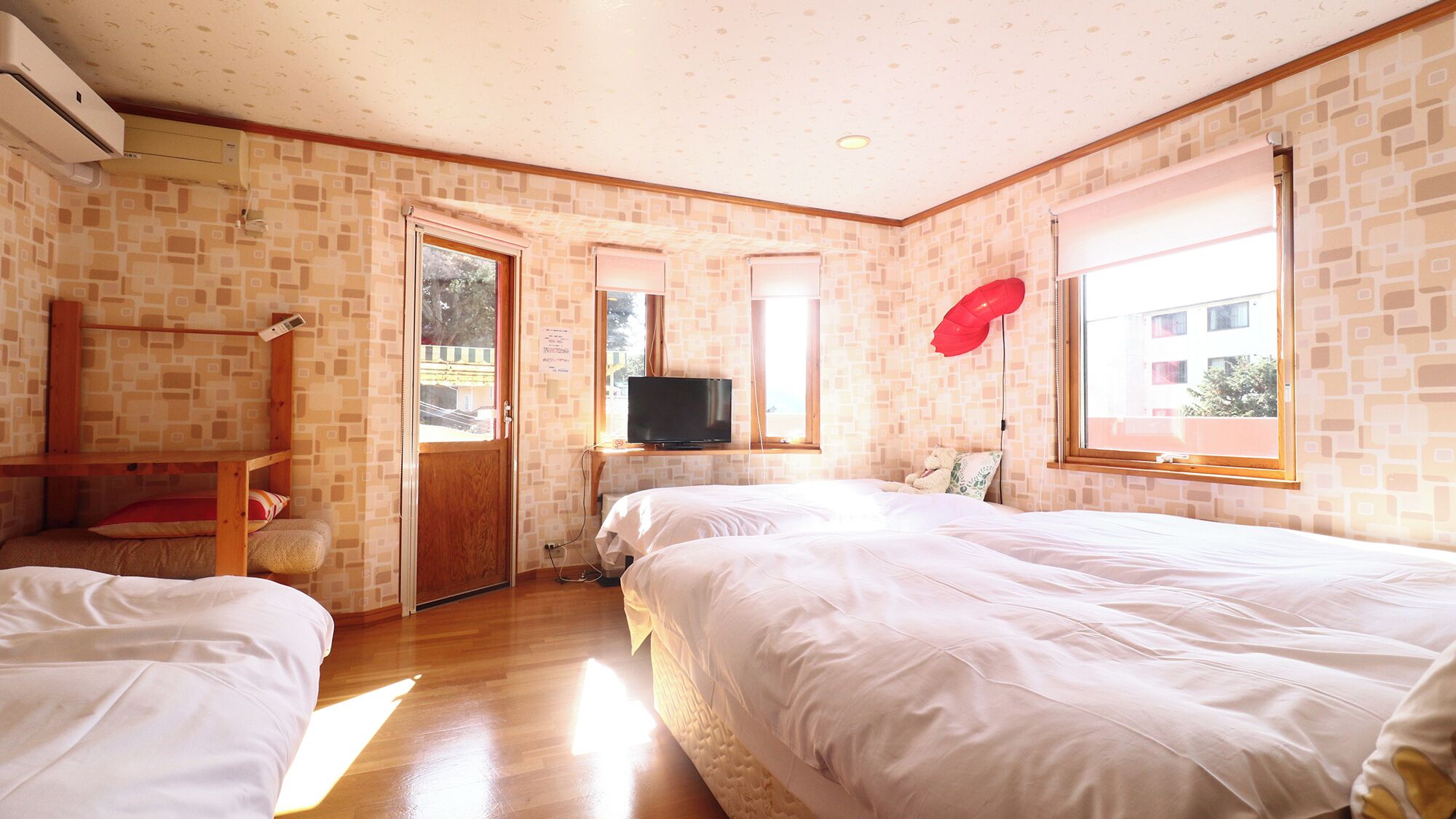 Quarto com duas camas, televisão e janela com vista para prédios.