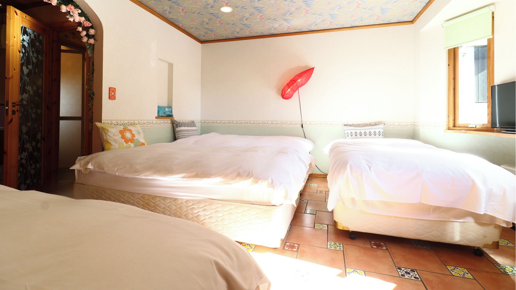 Quarto de hotel com duas camas, uma televisão e um leque decorativo vermelho.