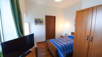 Quarto com cama, televisão, guarda-roupa de madeira, mesa de cabeceira e um quadro na parede.